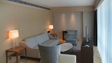 Quarto de hotel moderno com sofá, poltrona, mesa de centro e televisão de tela plana.