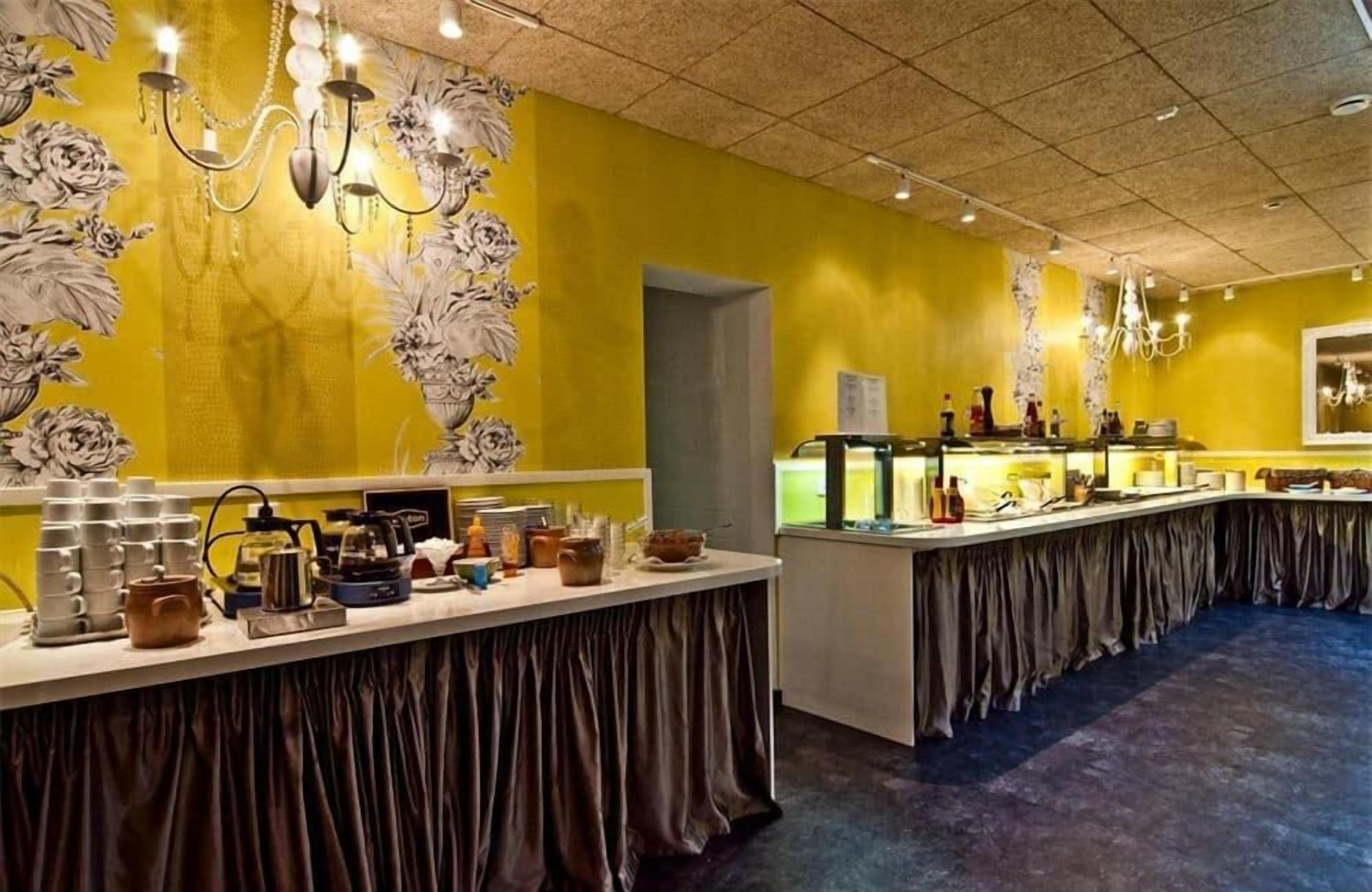 Disposição de buffet com parede amarela e papel de parede floral, um balcão comprido com diversos alimentos e um candelabro.