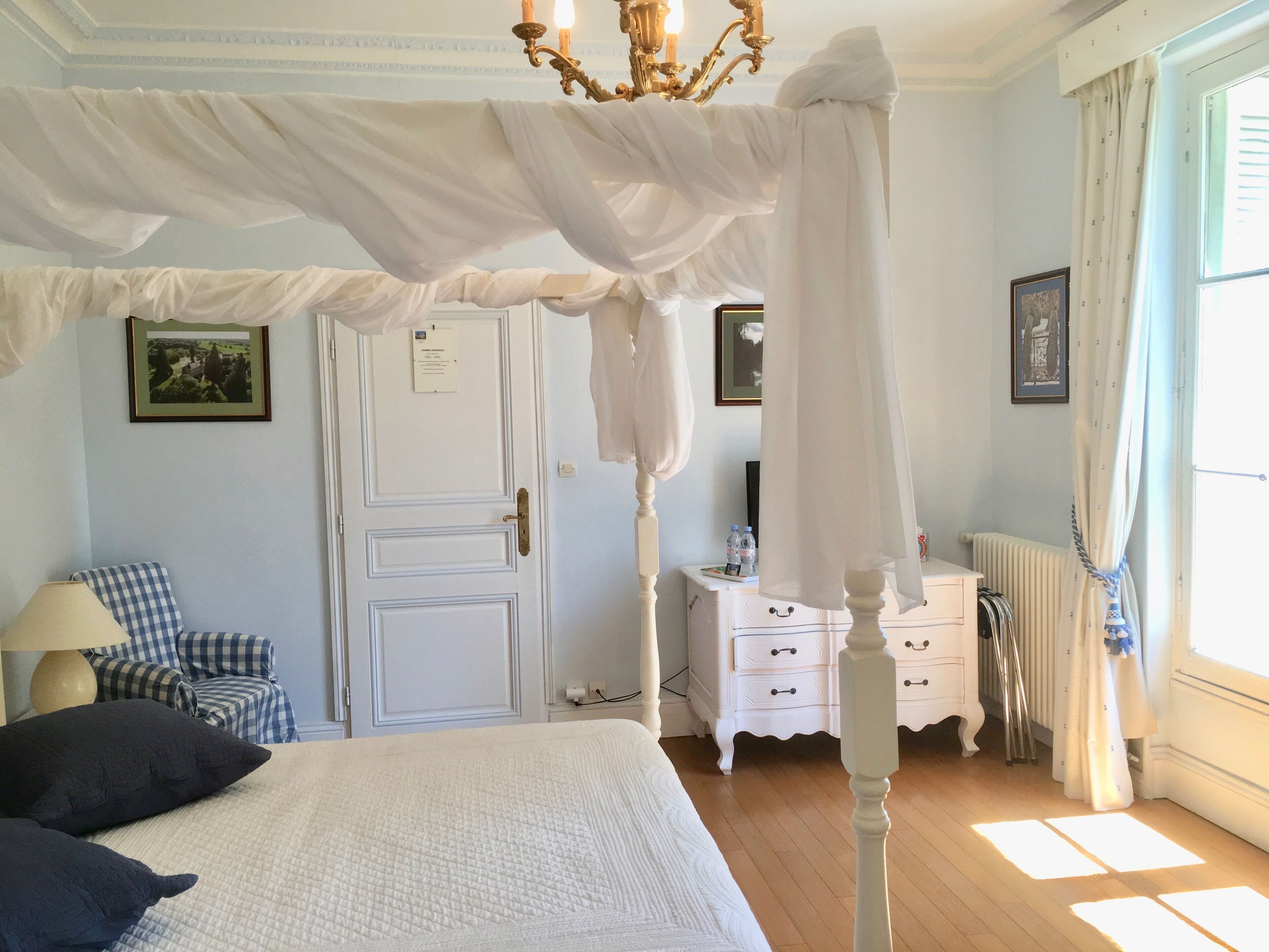 Quarto com cama de dossel, mesa de cabeceira com abajur, cômoda e radiador.