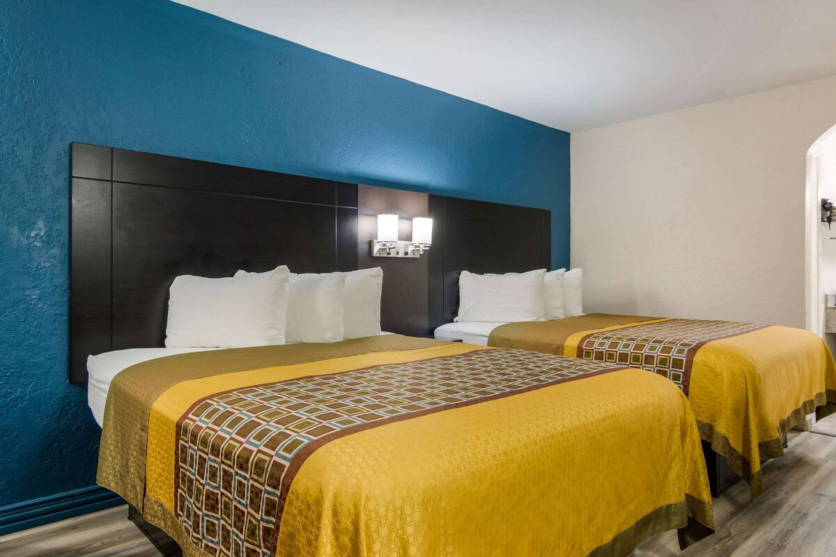 Quarto de hotel com duas camas, uma cabeceira escura e uma parede azul decorativa.