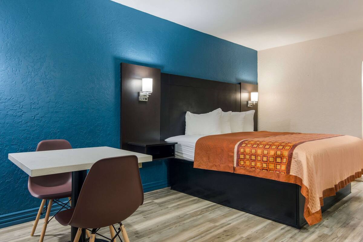Quarto de hotel com uma cama, uma escrivaninha e duas cadeiras.