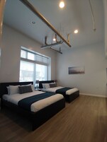 Quarto de hotel moderno com duas camas, uma janela grande com persianas, um quadro na parede e um lustre de design exclusivo.