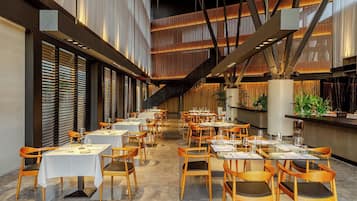 Uma ampla área de jantar com várias mesas e cadeiras, uma escadaria central e design de interiores moderno.