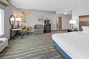 Quarto de hotel com cama, escrivaninha, cadeira e micro-ondas.