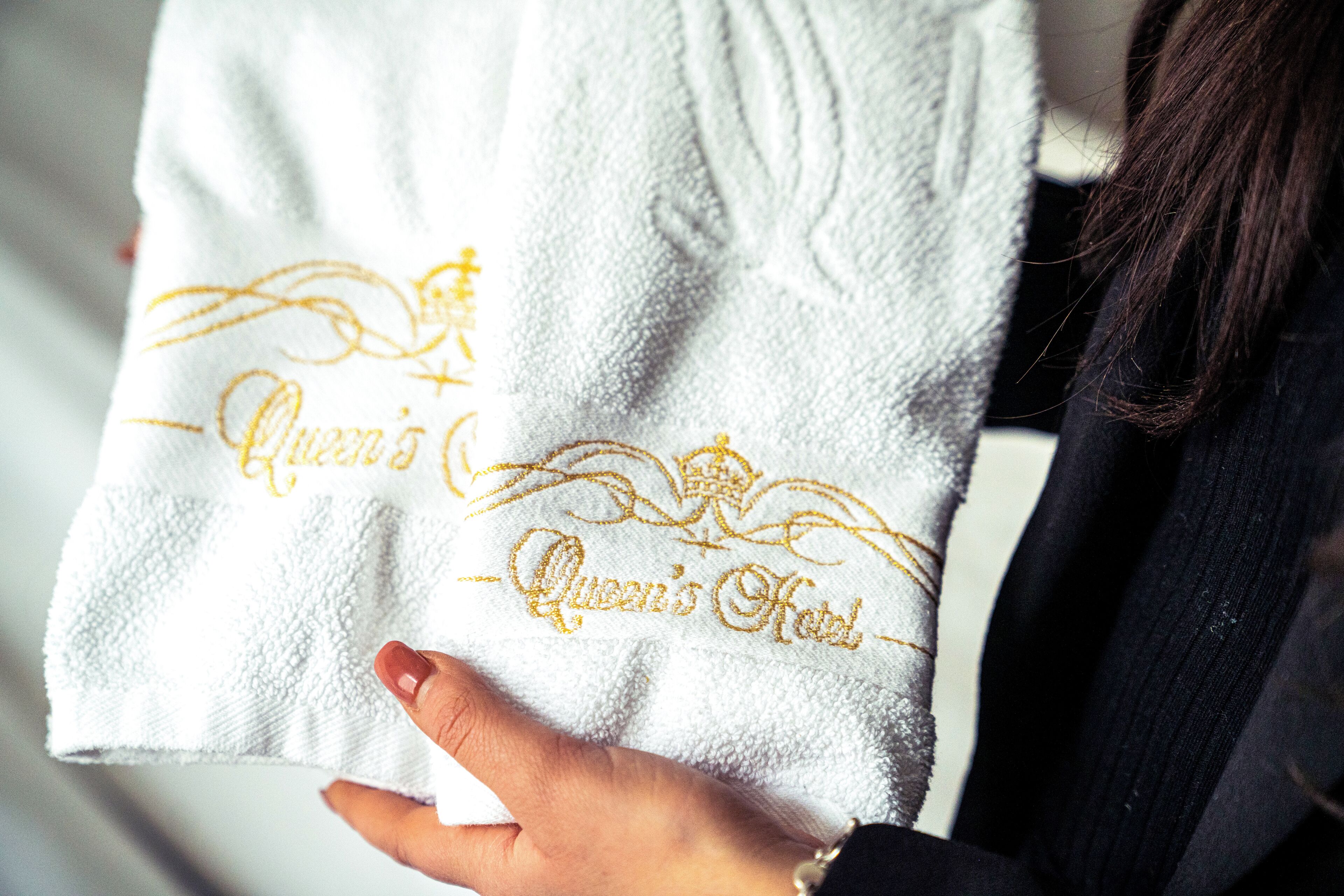 Toalha branca com bordado contendo a inscrição 'Queen's Hotel'.