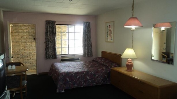 Quarto com cama, escrivaninha, cadeira, cômoda, janela com cortinas e abajur.