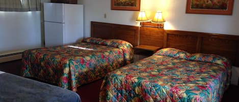Quarto de hotel com duas camas de solteiro, uma mesinha, um frigorífico e duas luminárias de parede.