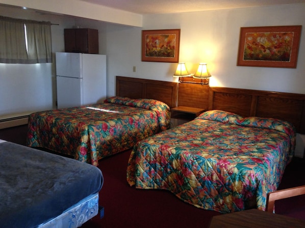 Quarto de hotel com duas camas de solteiro, uma mesinha, um frigorífico e duas luminárias de parede.