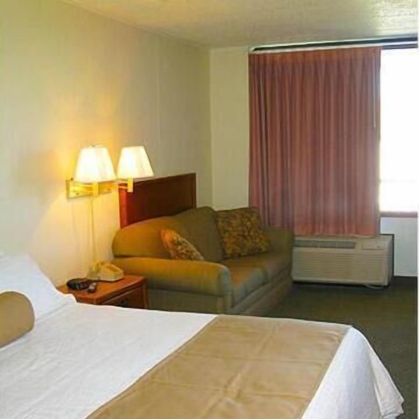 Quarto de hotel com cama, duas luminárias de cabeceira, um sofá, um telefone e um aparelho de ar condicionado.