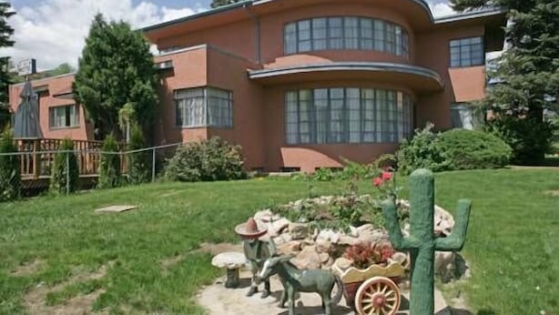 Um edifício grande e curvo de tijolo, com janelas amplas e um gramado bem cuidado com esculturas de jardim.