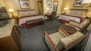 Quarto de hotel com duas camas, uma escrivaninha, uma cadeira, um sofá e uma mesinha.