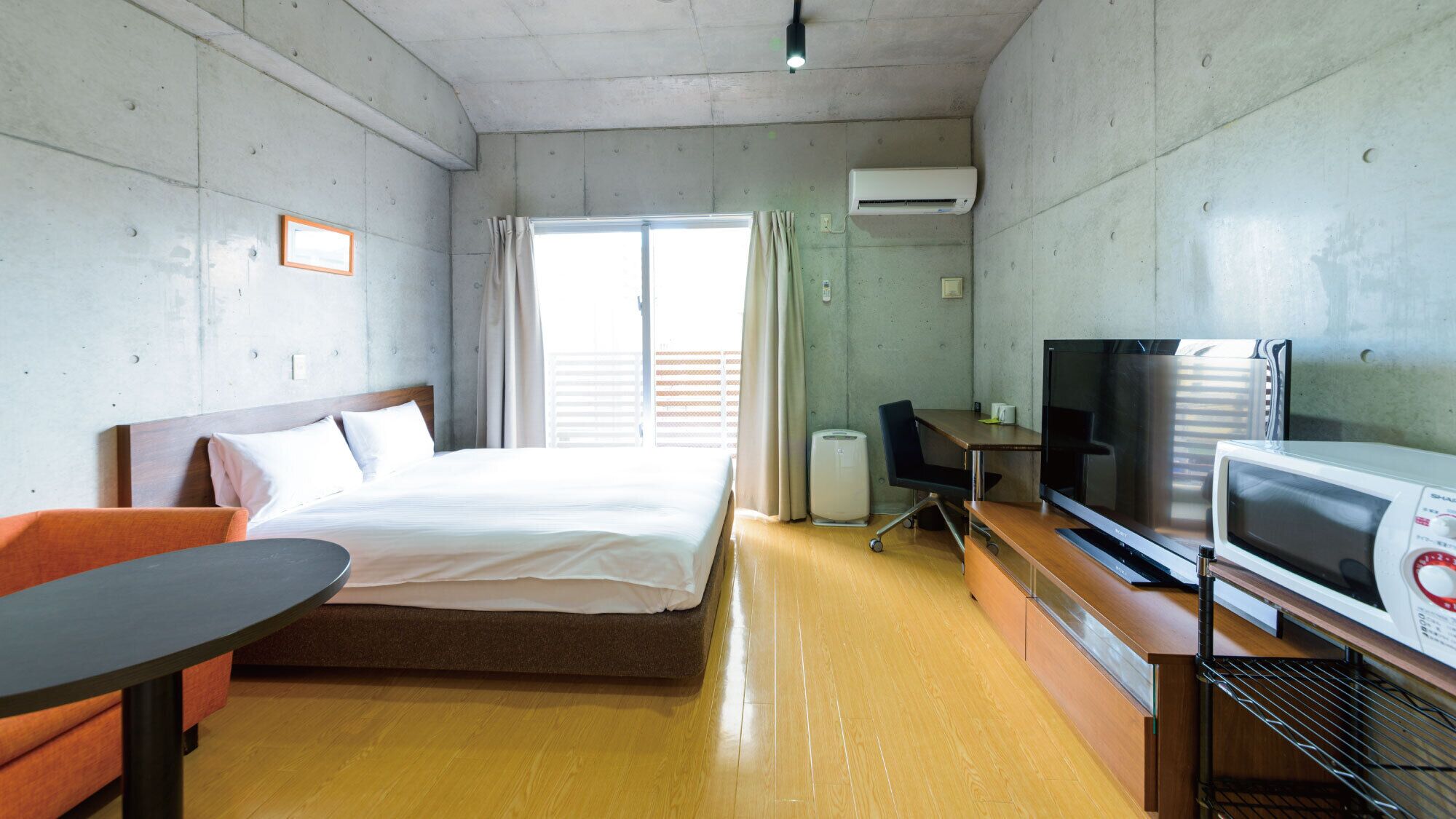 Quarto de hotel com cama, escrivaninha, televisão e ar condicionado.