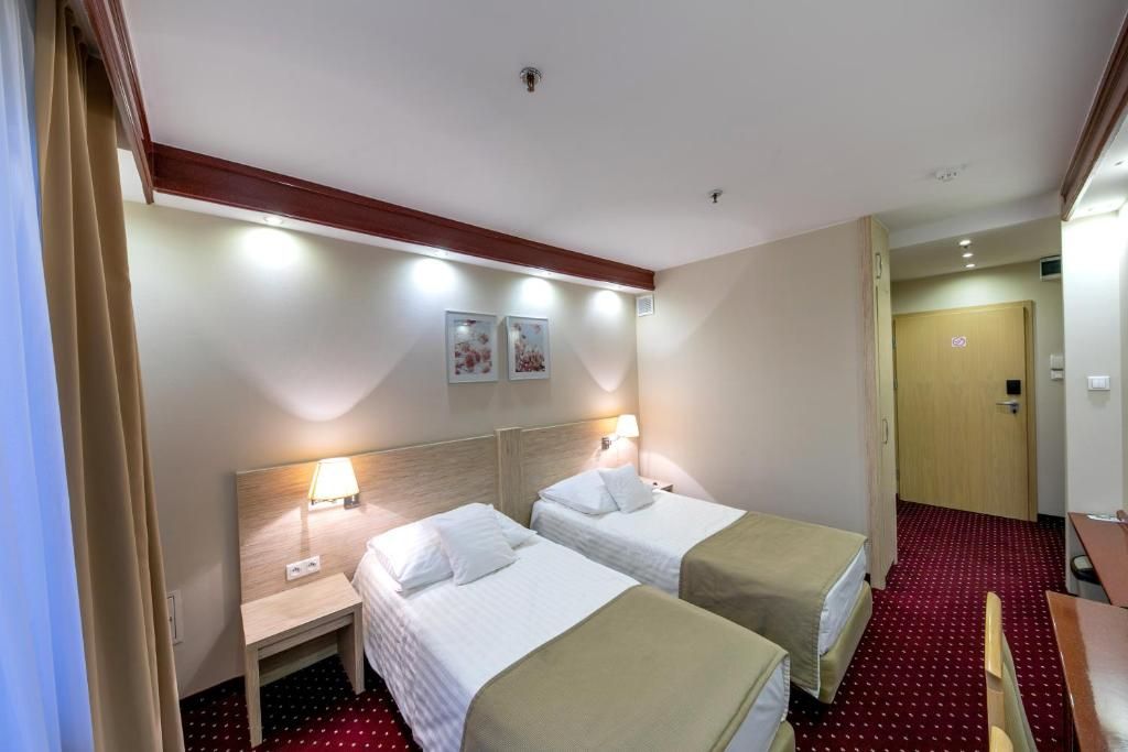 Quarto de hotel com duas camas, uma mesa, uma cadeira e uma porta.