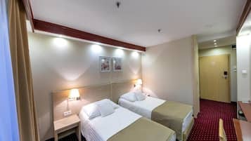 Quarto de hotel com duas camas, uma mesa, uma cadeira e uma porta.