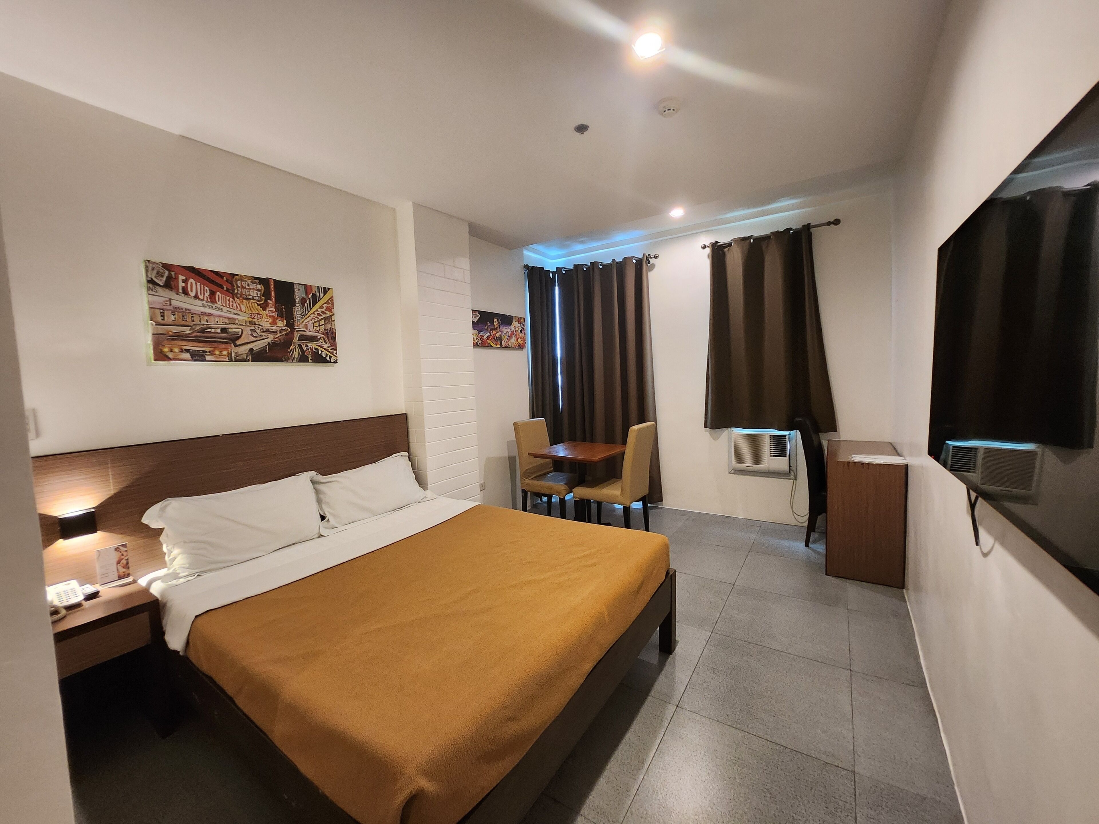 Quarto de hotel com cama, escrivaninha, cadeira, televisão e janela com cortinas.