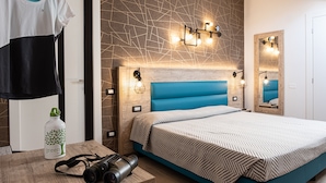 Quarto com colcha estampada, cabeceira azul e luminária fixada na parede.