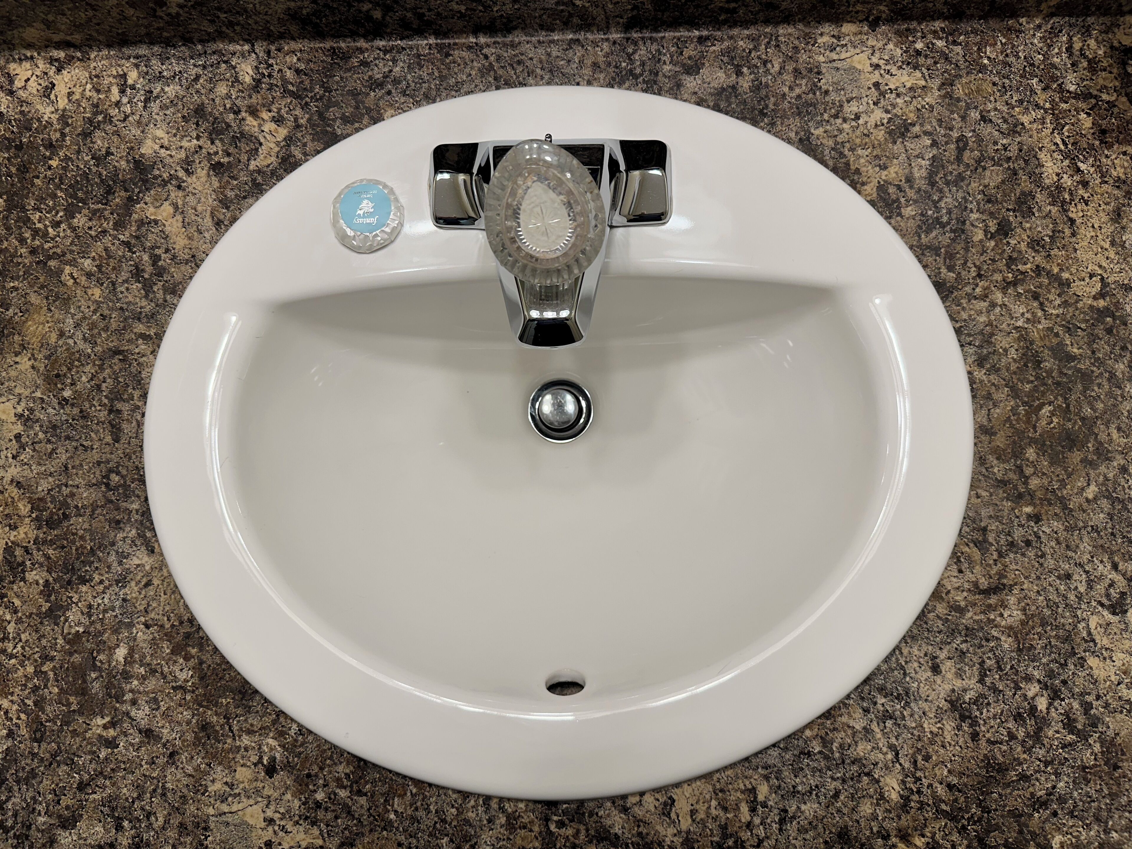 Uma pia branca com uma torneira cromada e um dispensador de sabão em bancada de granito.