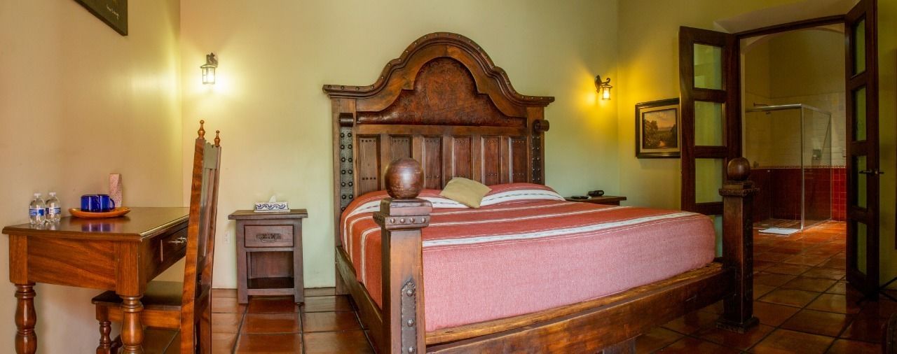Quarto com cama de madeira, mesas de cabeceira, escrivaninha e uma cadeira.