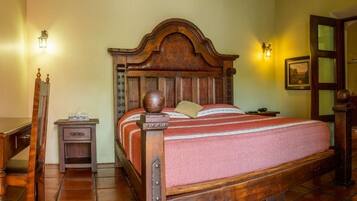 Quarto com cama de madeira, mesas de cabeceira, escrivaninha e uma cadeira.