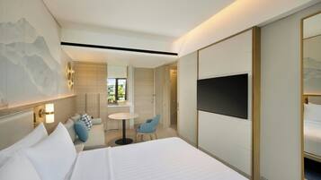 Quarto de hotel com uma cama grande, televisão, escrivaninha e vista para o exterior.