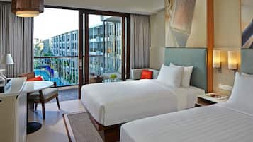 Quarto de hotel com duas camas, uma escrivaninha, uma cadeira, uma mesa de jantar e uma varanda com vista para edifícios.
