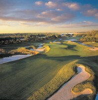 Um campo de golfe com obstáculos de água, bunkers de areia e mastro de sinalização.