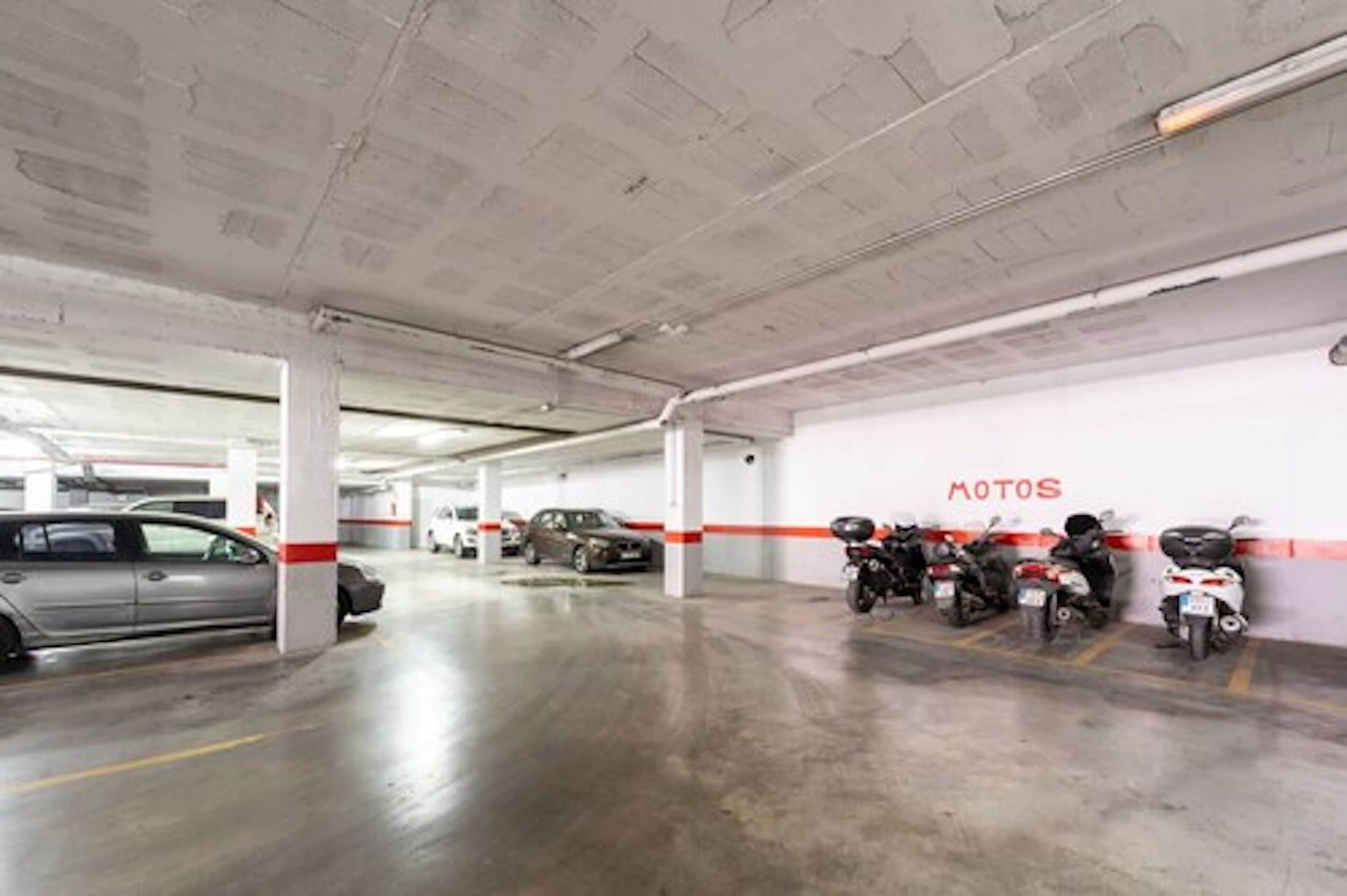 Uma garagem de estacionamento com pilares de concreto, um carro e motocicletas estacionadas.
