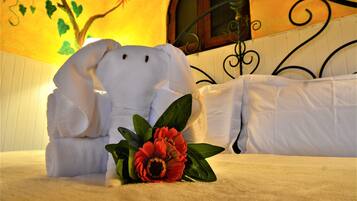 Uma cama com uma toalha branca dobrada em forma de elefante, uma flor vermelha e um painel decorativo com uma árvore e folhas.