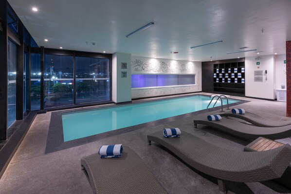 Piscina interior moderna com espreguiçadeiras e vista para o horizonte da cidade.