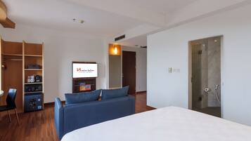 Quarto de hotel com cama, sofá, televisão, minibar e área de chuveiro.