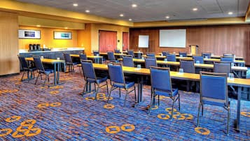 Uma sala de conferências com várias mesas e cadeiras, uma tela de projeção e um púlpito para apresentações.