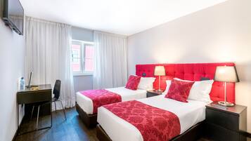 Quarto de hotel com duas camas, uma escrivaninha, uma cadeira, uma televisão e uma janela com cortinas.