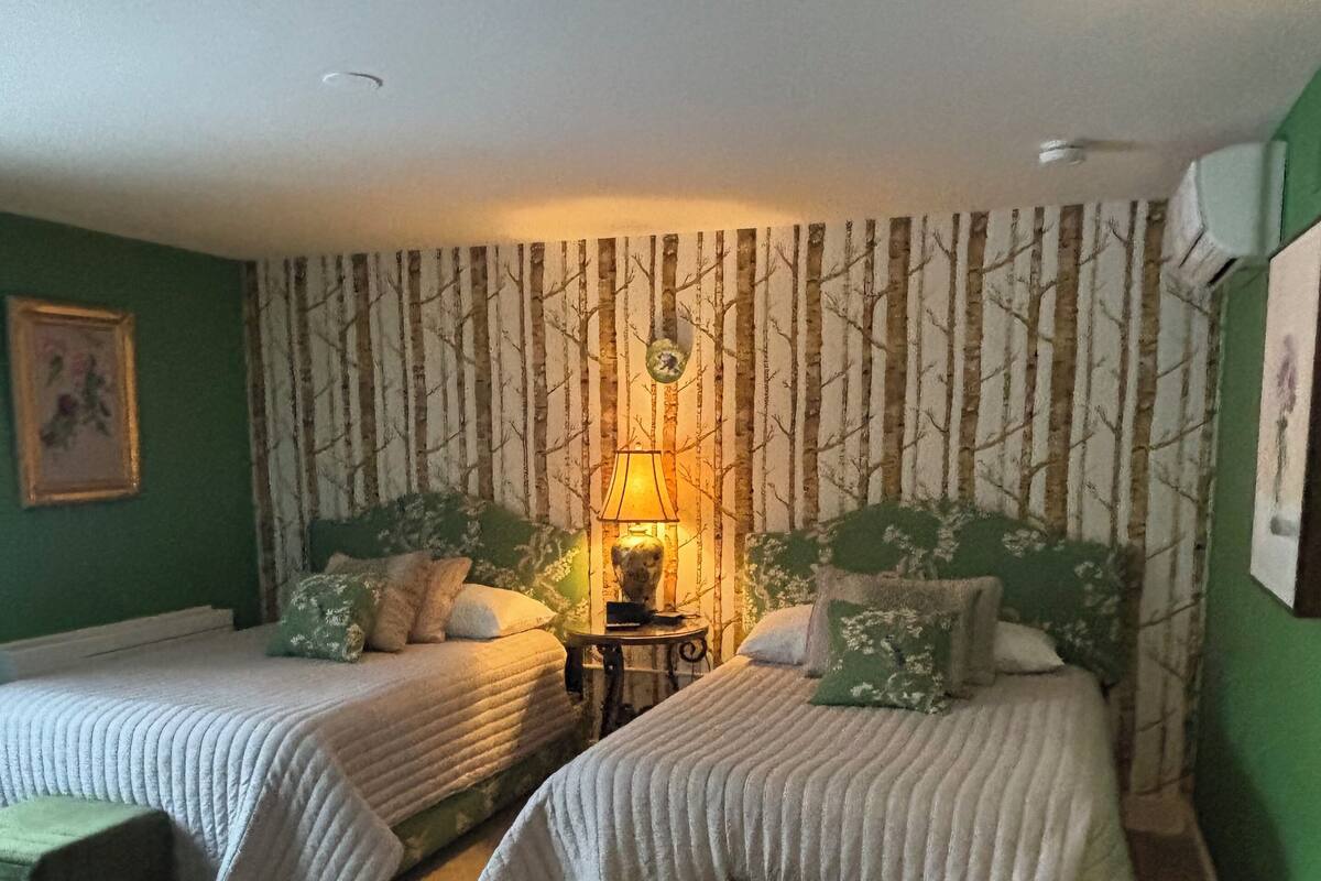 Quarto com duas camas, uma mesa pequena e um abajur.