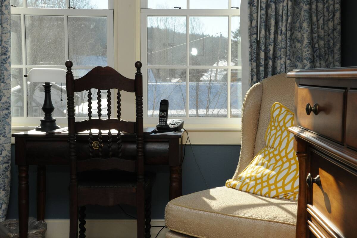 Um quarto com uma cadeira de madeira, uma mesinha de cabeceira e um aparador.