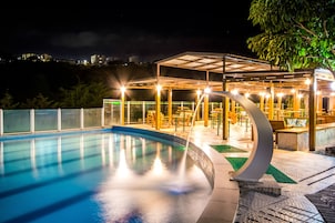 Piscina com área de estar coberta e vista para o horizonte urbano ao fundo.