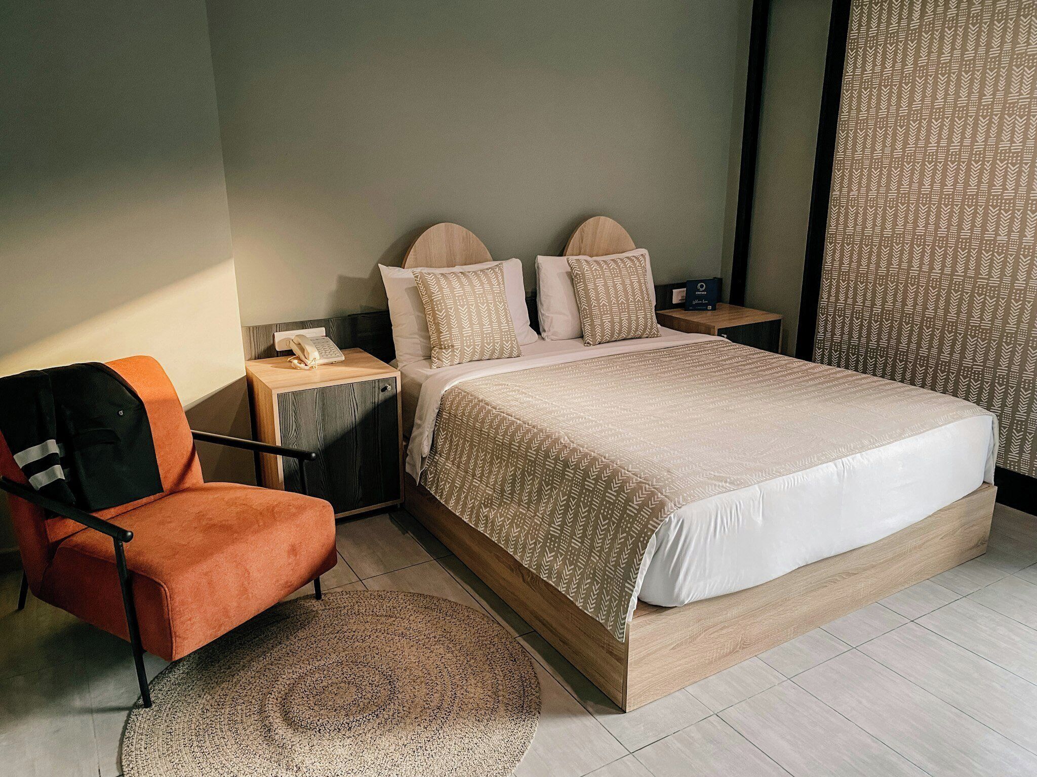 Quarto de hotel com uma cama, uma cadeira, uma mesa de cabeceira e cortina estampada.