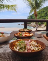 Uma mesa com tigelas de comida, vista para a praia e uma palmeira.