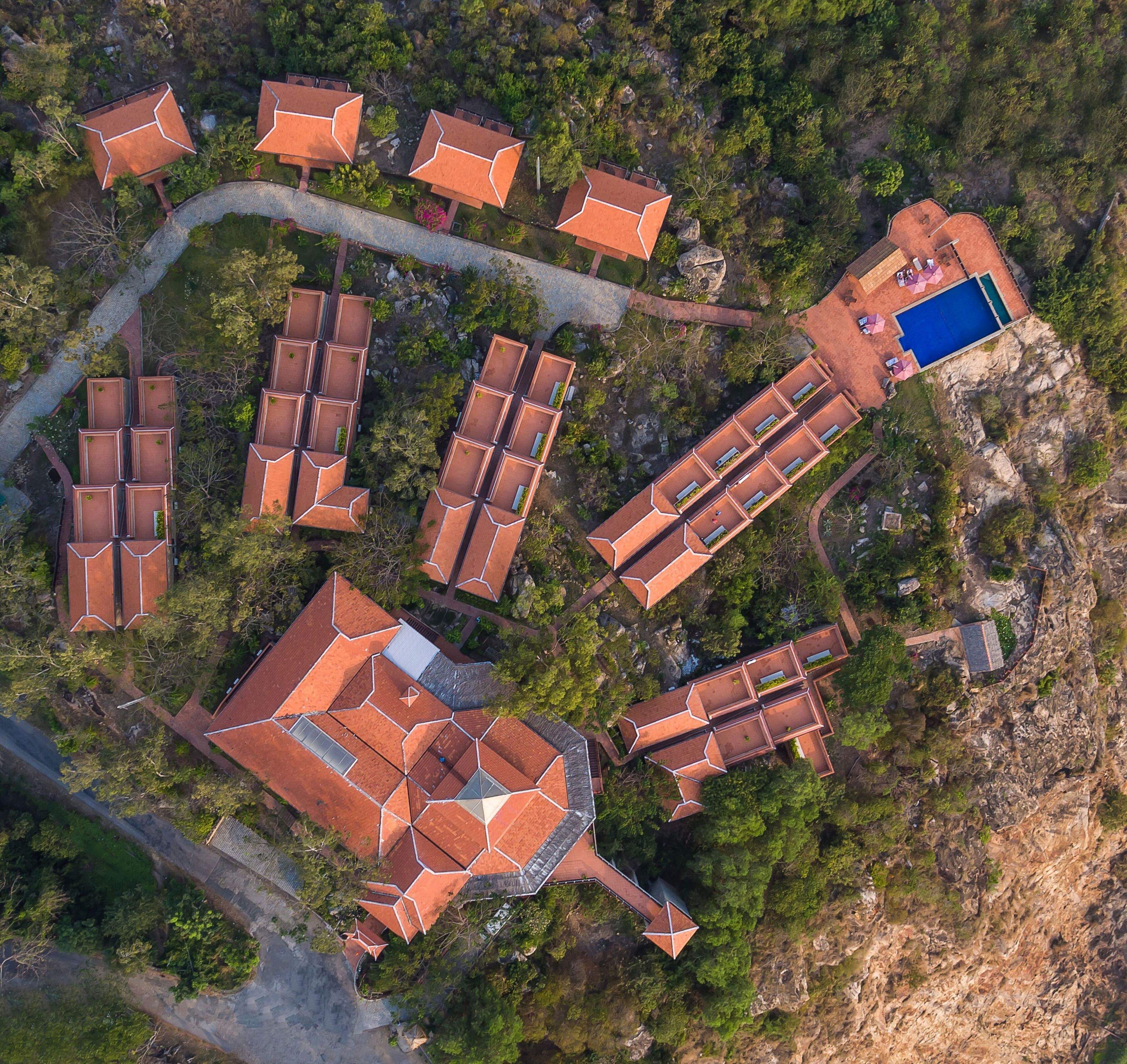 Vista aérea de um resort com vários edifícios, piscina e vegetação ao redor.