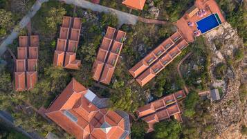 Vista aérea de um resort com vários edifícios, piscina e vegetação ao redor.