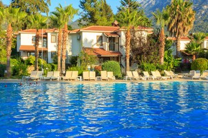 Piscina com espreguiçadeiras e um edifício com telhado de telhas vermelhas.