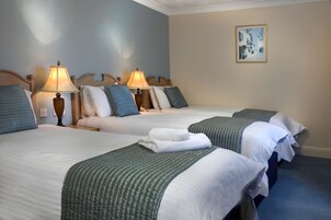 Quarto de hotel com duas camas, cada uma com luminária, almofadas e cobertor.