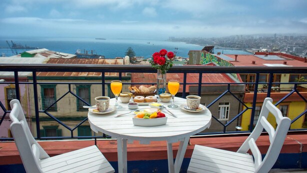 Varanda com mesa posta para o café da manhã, com vista para a paisagem urbana costeira.