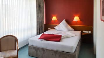 Quarto de hotel com uma cama, duas luminárias de cabeceira, uma cadeira e uma janela com persianas.