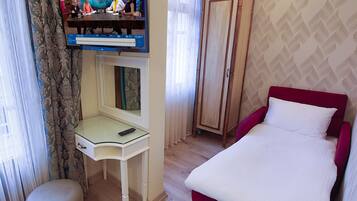 Quarto de hotel com cama, televisão presa na parede, escrivaninha com cadeira, guarda-roupa e um banquinho.