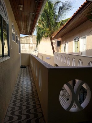 Um corredor com piso estampado, área coberta com uma palmeira e um edifício com janelas em arco e uma placa indicando um restaurante.