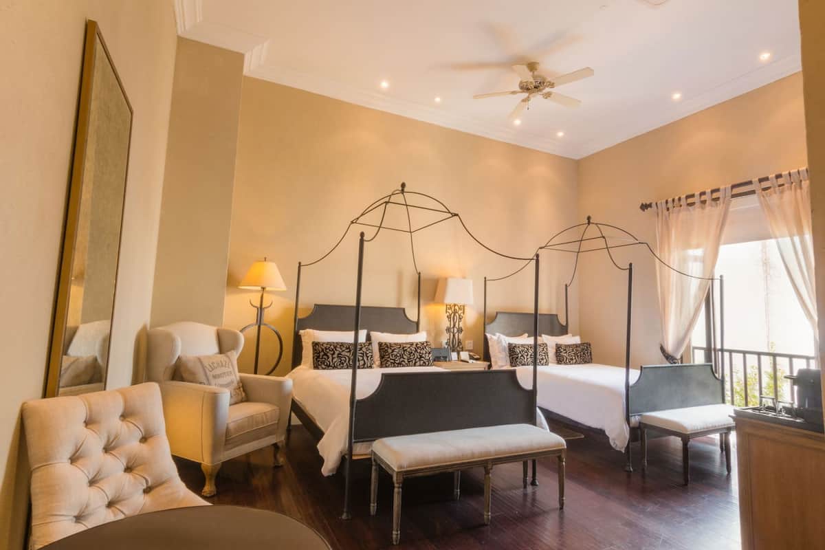 Uma cama com dossel e cortina, um chaise longue, uma mesa de cabeceira com abajur e um espelho grande.