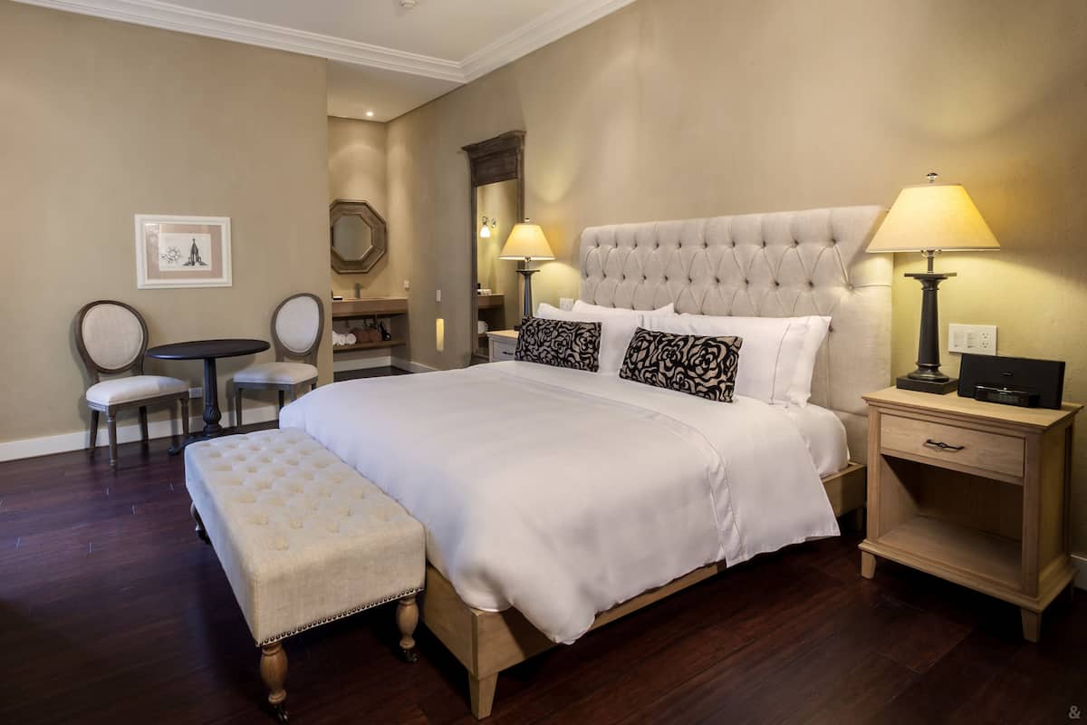Quarto de hotel com uma cama grande, duas mesas de cabeceira, um banco e uma cadeira.