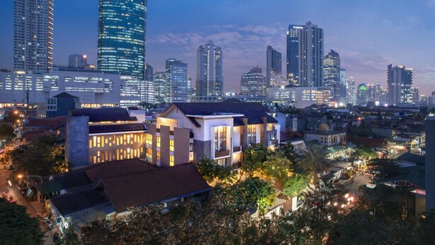 Paisagem urbana ao entardecer, com edifícios modernos e arranha-céus, incluindo um imponente arranha-céu curvo, e áreas residenciais com casas bem iluminadas.