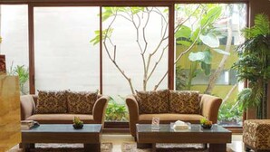 Uma sala de estar com sofá, duas mesinhas de centro e uma janela grande com vista para o verde.