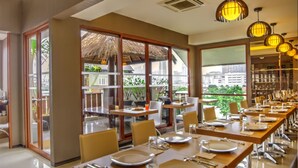 Restaurante com mesas longas, cadeiras e telhado de palha.